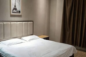 Quarto de hotel com uma cama, mesa de cabeceira, quadro com a Torre Eiffel e uma janela com cortinas.