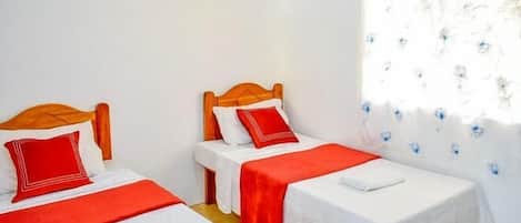 Quarto com duas camas de solteiro, cada uma com cabeceira de madeira, roupa de cama branca e detalhes em vermelho.
