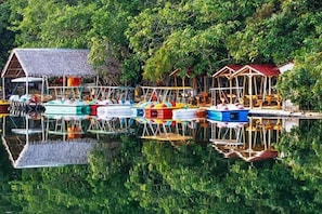 Um cais tranquilo à beira do lago, com várias embarcações, estruturas de madeira e vegetação exuberante.