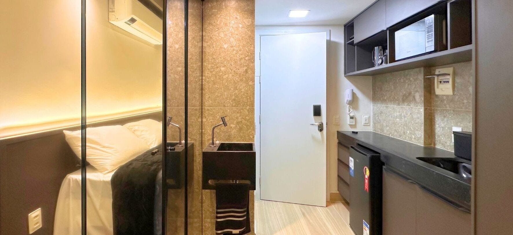 Quarto de hotel com cama, banheiro com chuveiro, pia e micro-ondas.