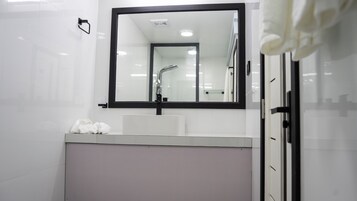 Uma casa de banho moderna com uma sanita branca, um espelho grande e um chuveiro visível no reflexo.
