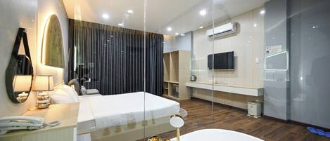Quarto de hotel moderno com uma cama grande, banheiro separado com banheira, toucador com espelho e TV de tela plana na parede.