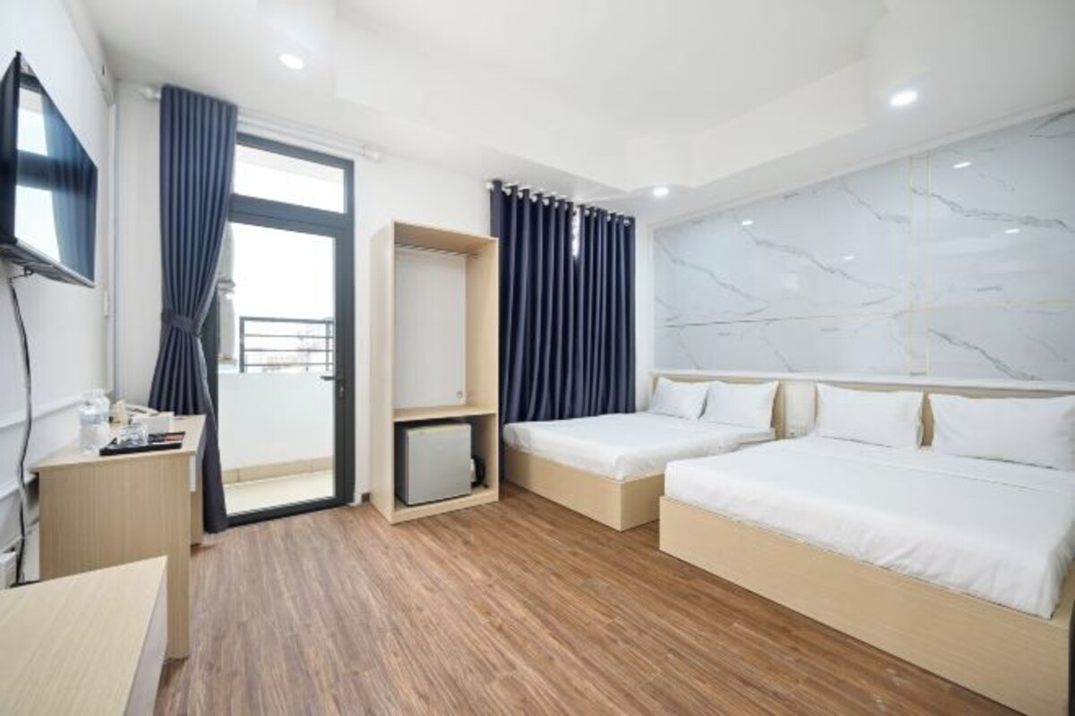 Quarto de hotel moderno com piso de madeira, uma cama grande, uma escrivaninha e uma televisão.