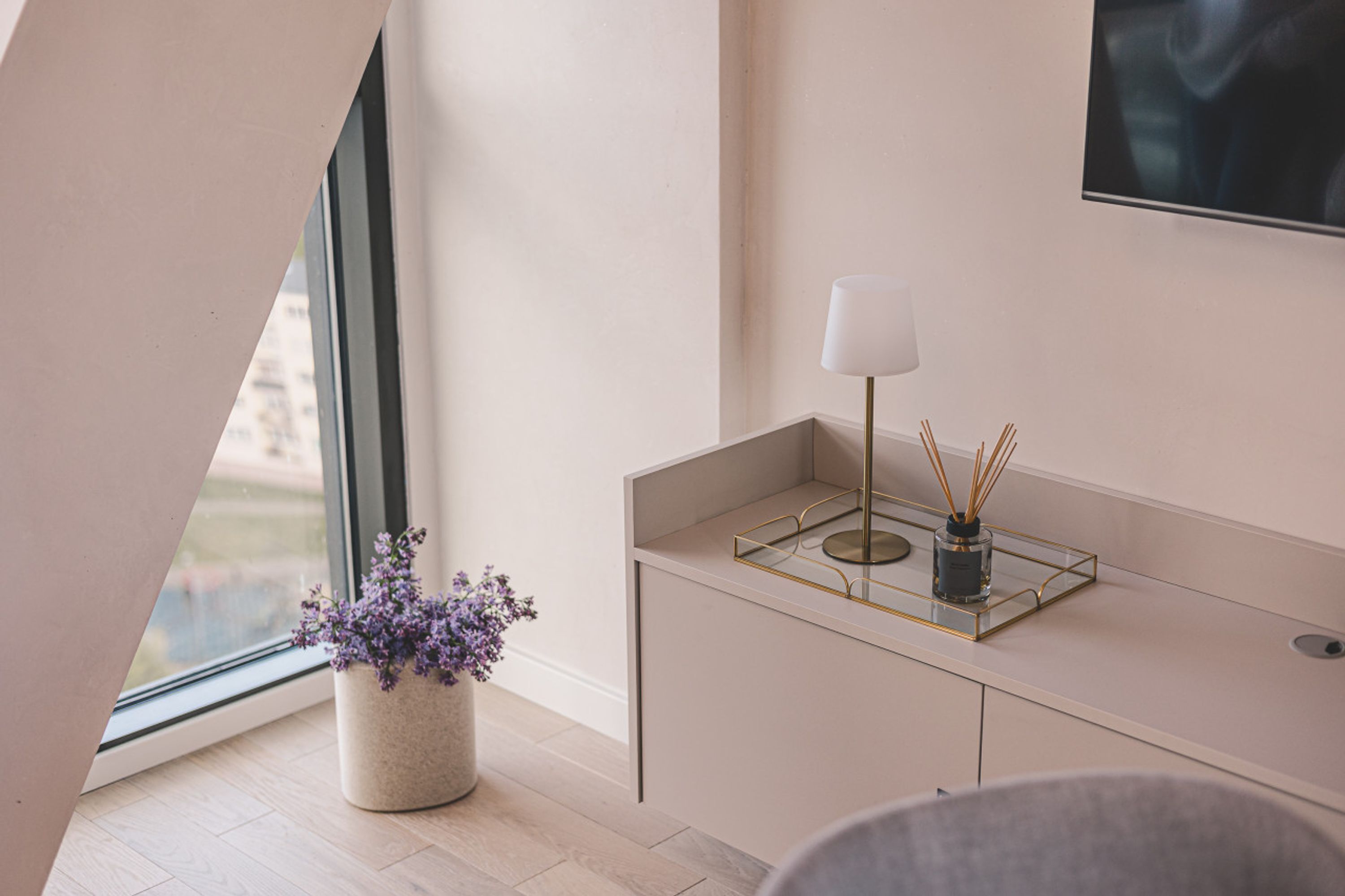 Quarto moderno com uma janela grande, uma planta em vaso, uma luminária e um suporte de vidro sobre um console minimalista.