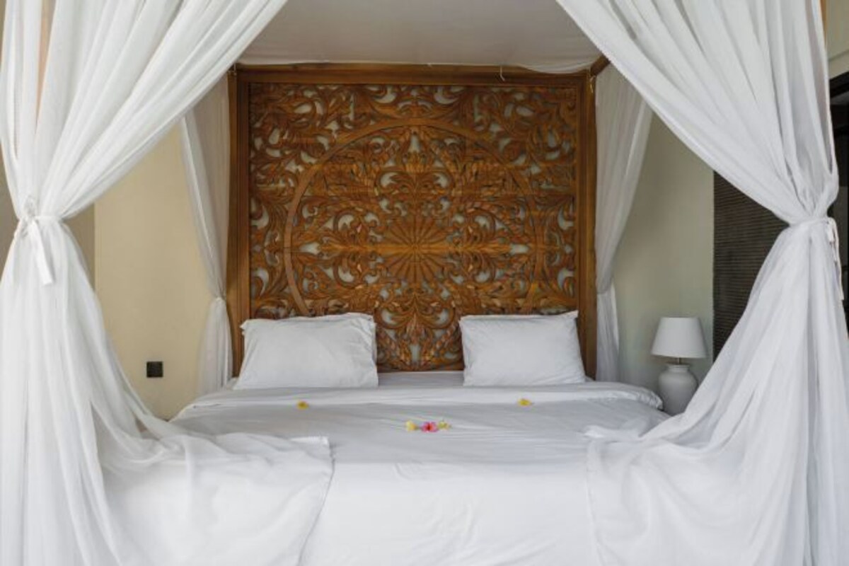Uma cama com dossel, cabeceira de madeira e duas almofadas.