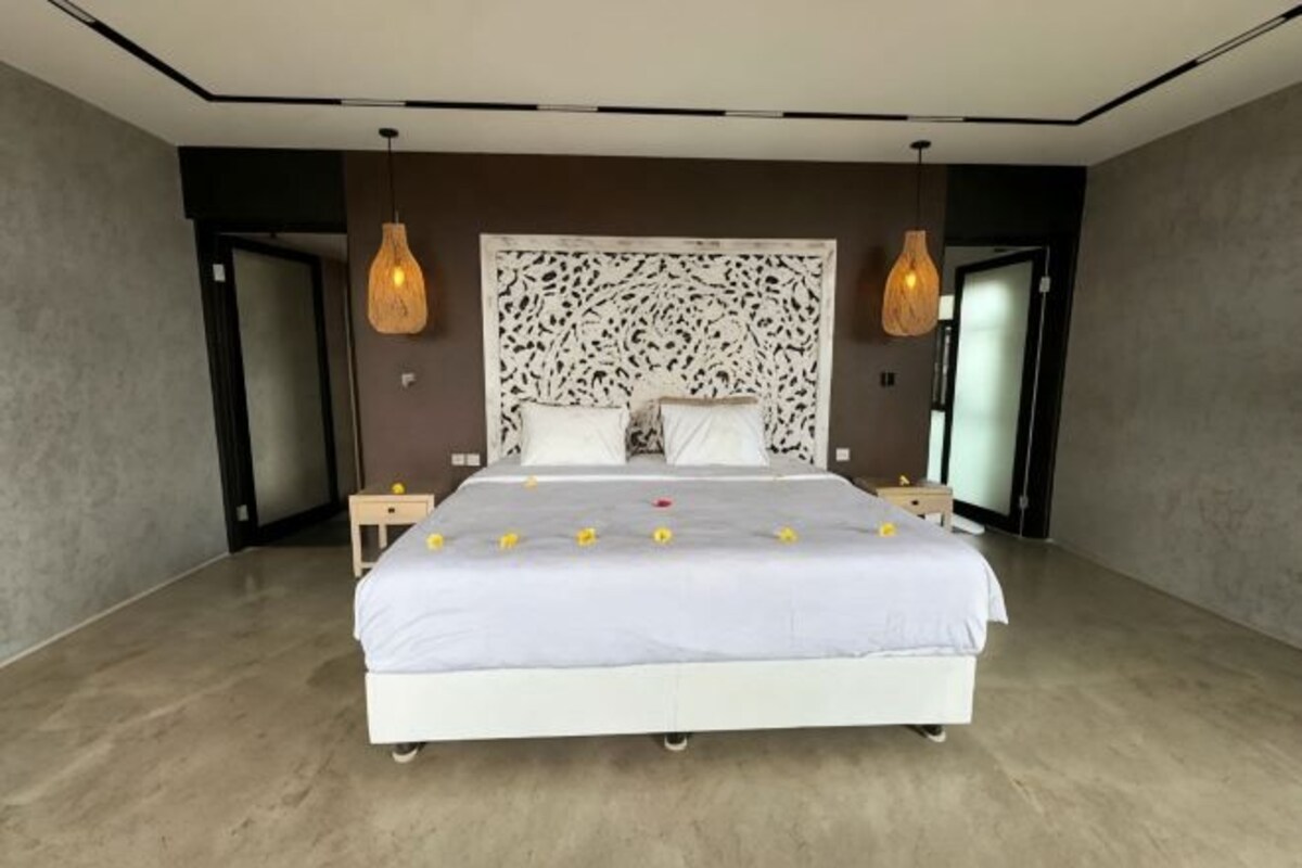 Quarto moderno com uma cama grande, duas mesas de cabeceira e uma cabeceira decorativa.