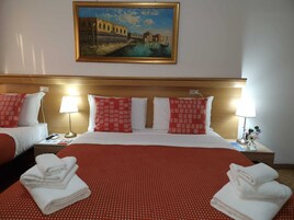 Quarto de hotel com uma cama grande, duas mesas de cabeceira, um quadro de uma cena de canal e um edredom com padrão vermelho e branco.