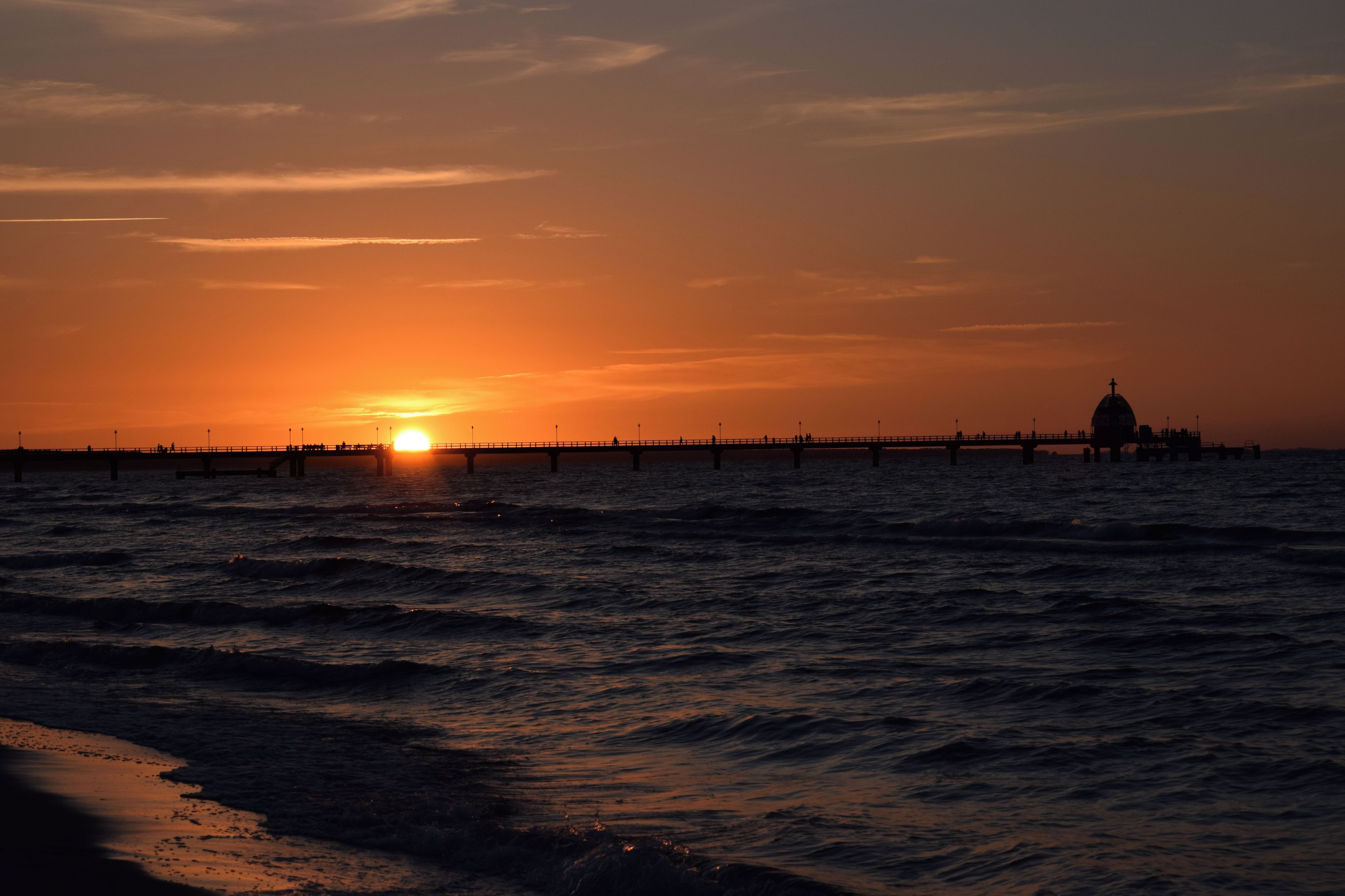 Um pôr do sol sobre a água, com um cais que se estende até o mar.