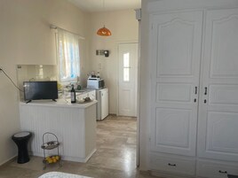 Uma cozinha com televisão, pia e micro-ondas. Há uma porta que dá para outro quarto.