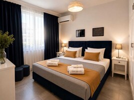 Quarto de hotel com uma cama grande, duas mesas de cabeceira, um criado-mudo e uma escrivaninha, além de uma janela com cortinas.