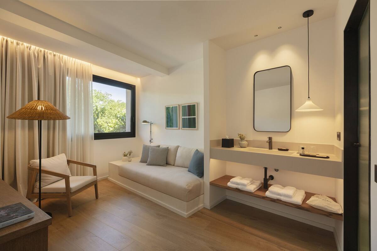 Uma casa de banho moderna com sofá, candeeiro, espelho e prateleira com toalhas.