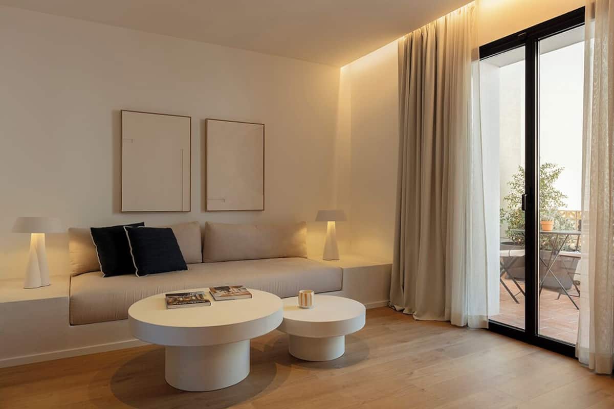Uma sala de estar moderna com um sofá, duas mesas laterais e um vão de vidro que dá para uma área externa.