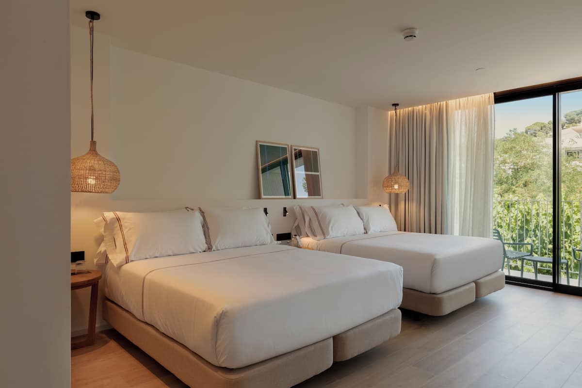 Quarto moderno com duas camas, uma janela grande com cortinas e um lustre.