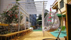 Um deck de madeira com uma cadeira suspensa, uma pérgula e uma parede de pedra.