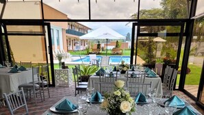 Uma área de refeições com mesas redondas preparadas para uma refeição, cadeiras e um arranjo floral central.