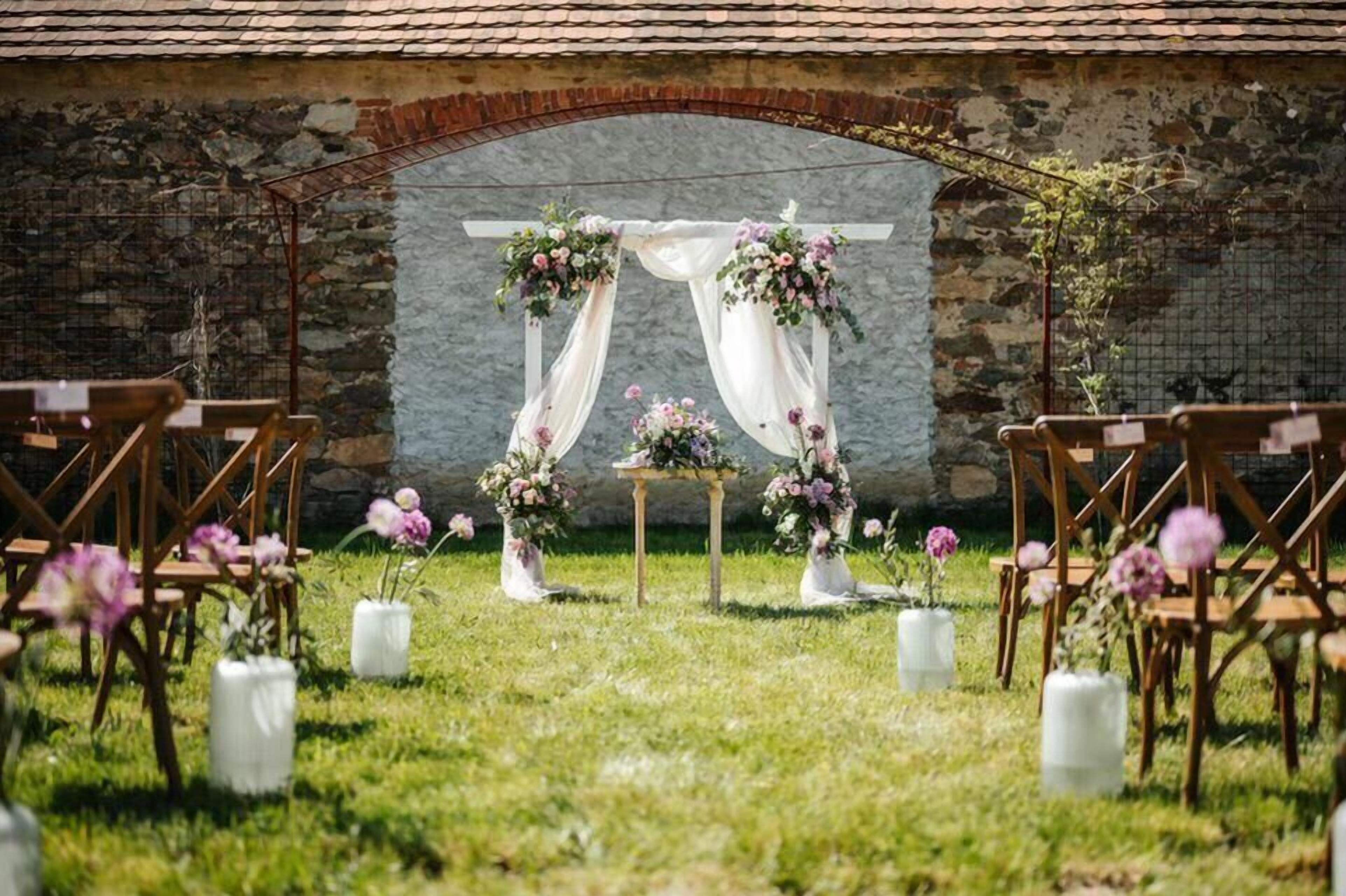Decoração de casamento ao ar livre com arco de pedra, cortinas brancas e arranjos florais.