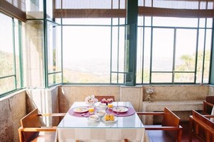 Uma sala de jantar com mesa posta para o café da manhã, grandes janelas com vista para a paisagem e um banco ao longo da parede.