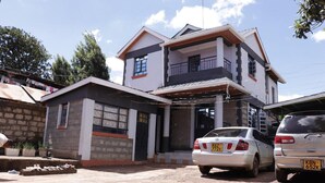Uma casa de dois andares com varanda, garagem e entrada para carros com dois veículos estacionados.