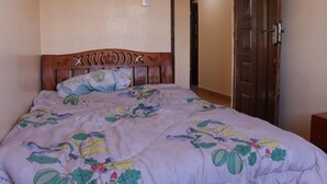 Quarto com cabeceira de madeira, roupa de cama florida e porta de madeira.