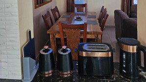 Uma sala de jantar com uma mesa e cadeiras de madeira, uma luminária no teto e eletrodomésticos na bancada.