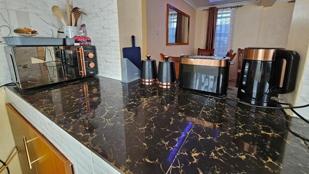 Uma cozinha moderna com bancada de mármore preto, micro-ondas embutido, máquina de café e torradeira.