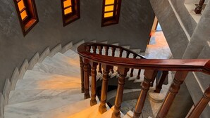 Uma escadaria em espiral com degraus de mármore e balaústres de madeira, que leva a um patamar com três janelas em arco.
