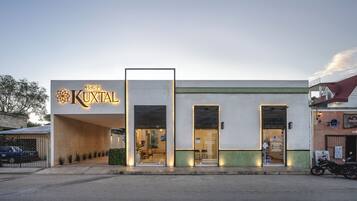 Um hotel chamado "Hotel Kuxtal" com fachada moderna, grandes janelas e entrada visível.