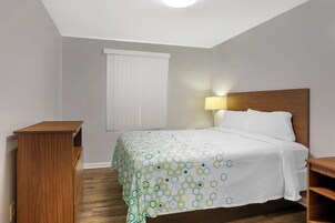 Quarto de hotel com cama, mesa de cabeceira, mesinha de madeira, janela com persianas e luminária fixada na parede.