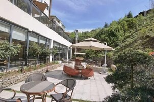 Um pátio externo com assentos, uma mesa e um grande guarda-sol.