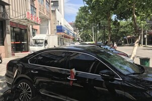 Um carro preto estacionado em uma rua da cidade, com edifícios e árvores ao fundo.