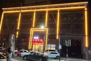 Um edifício com luzes de néon iluminadas, um estacionamento com vários carros e uma entrada visível.