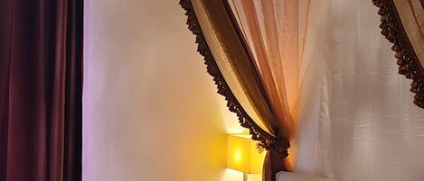 Uma cama com dossel, uma mesa de cabeceira com abajur e um aparelho de ar condicionado na parede.