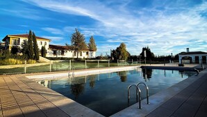 Piscina com vista clara da área circundante, incluindo um edifício com telhado em azulejos e um jardim cercado.