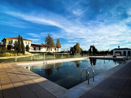 Piscina com vista clara da área circundante, incluindo um edifício com telhado em azulejos e um jardim cercado.