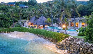 Um resort com piscina, espreguiçadeiras e construções com telhados de palha.