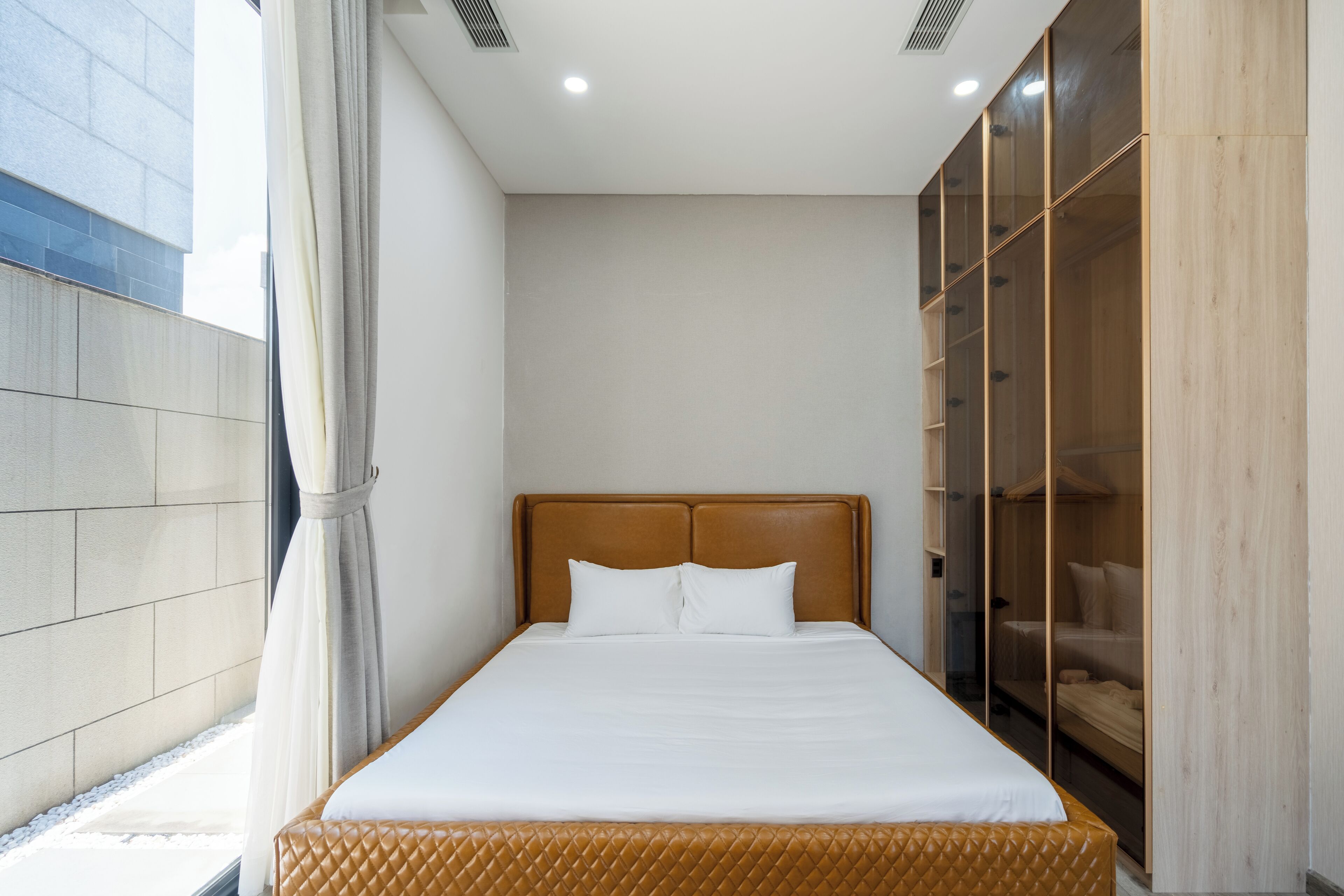 Quarto de hotel moderno com uma cama grande, um guarda-roupa de madeira e vista para o exterior.