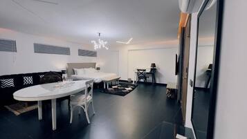 Quarto de hotel moderno com cama, mesa de jantar com cadeiras, escrivaninha e luminária no teto.