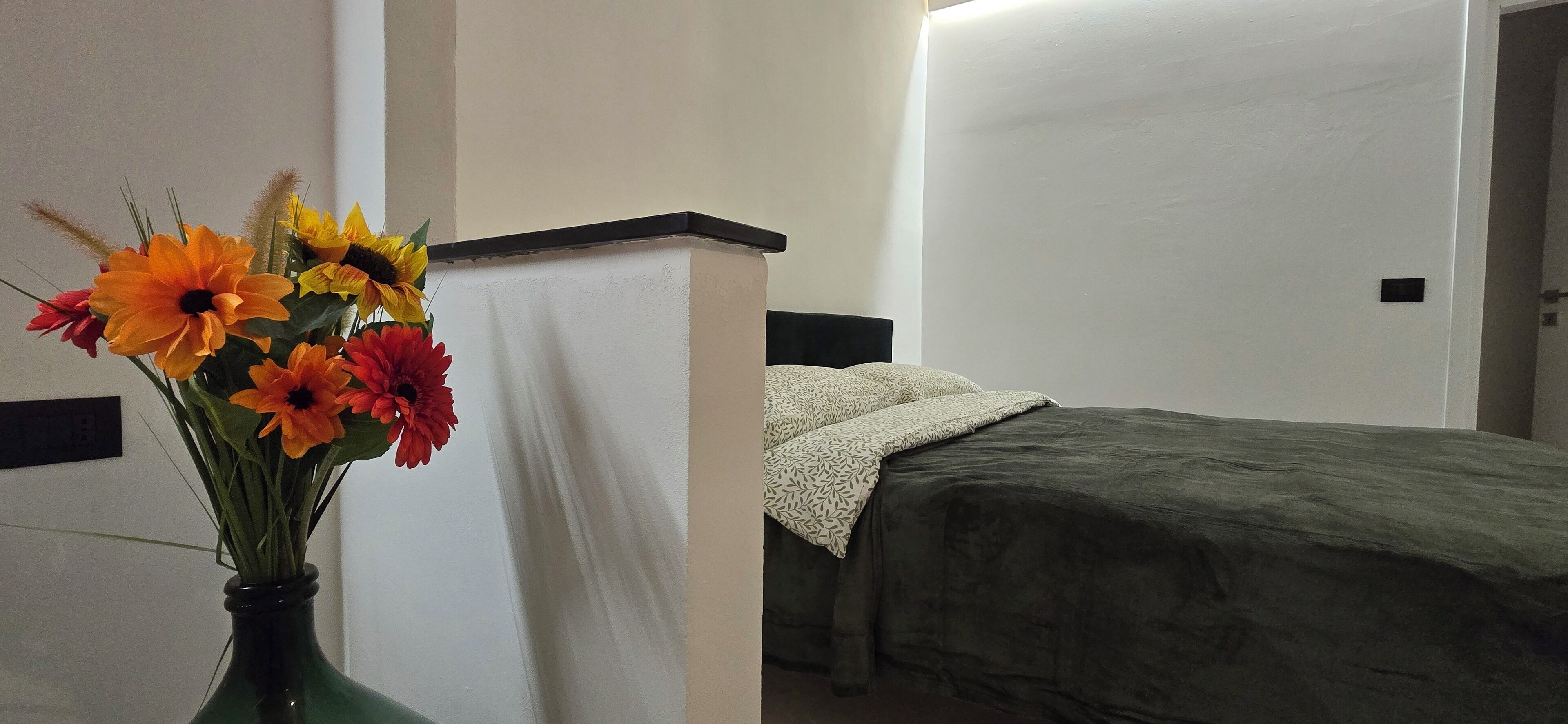 Quarto de hotel com cama, mesa de cabeceira e um vaso com flores.