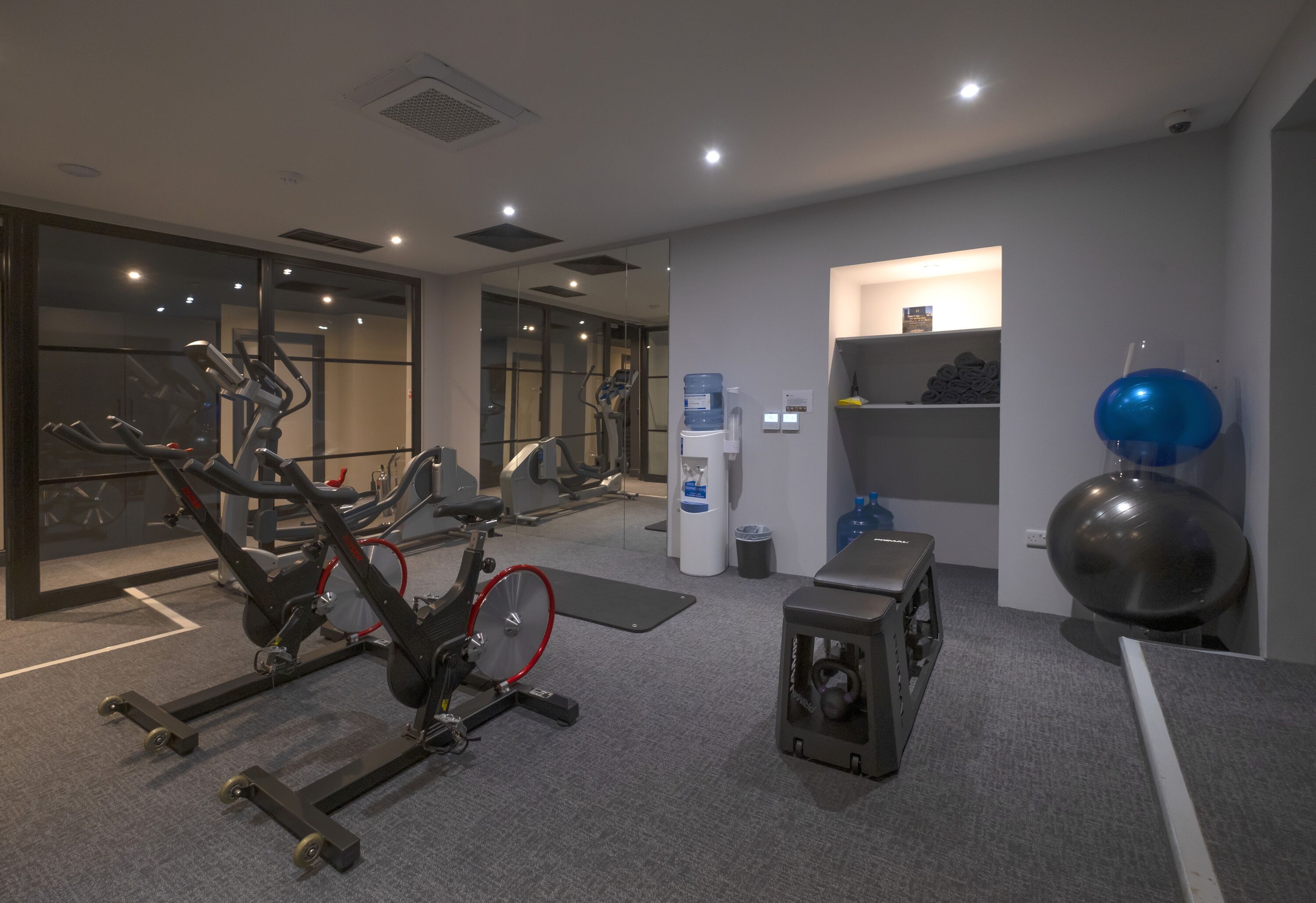 Uma academia com equipamentos de exercícios, bebedouro e espelho.