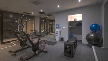 Uma academia com equipamentos de exercícios, bebedouro e espelho.