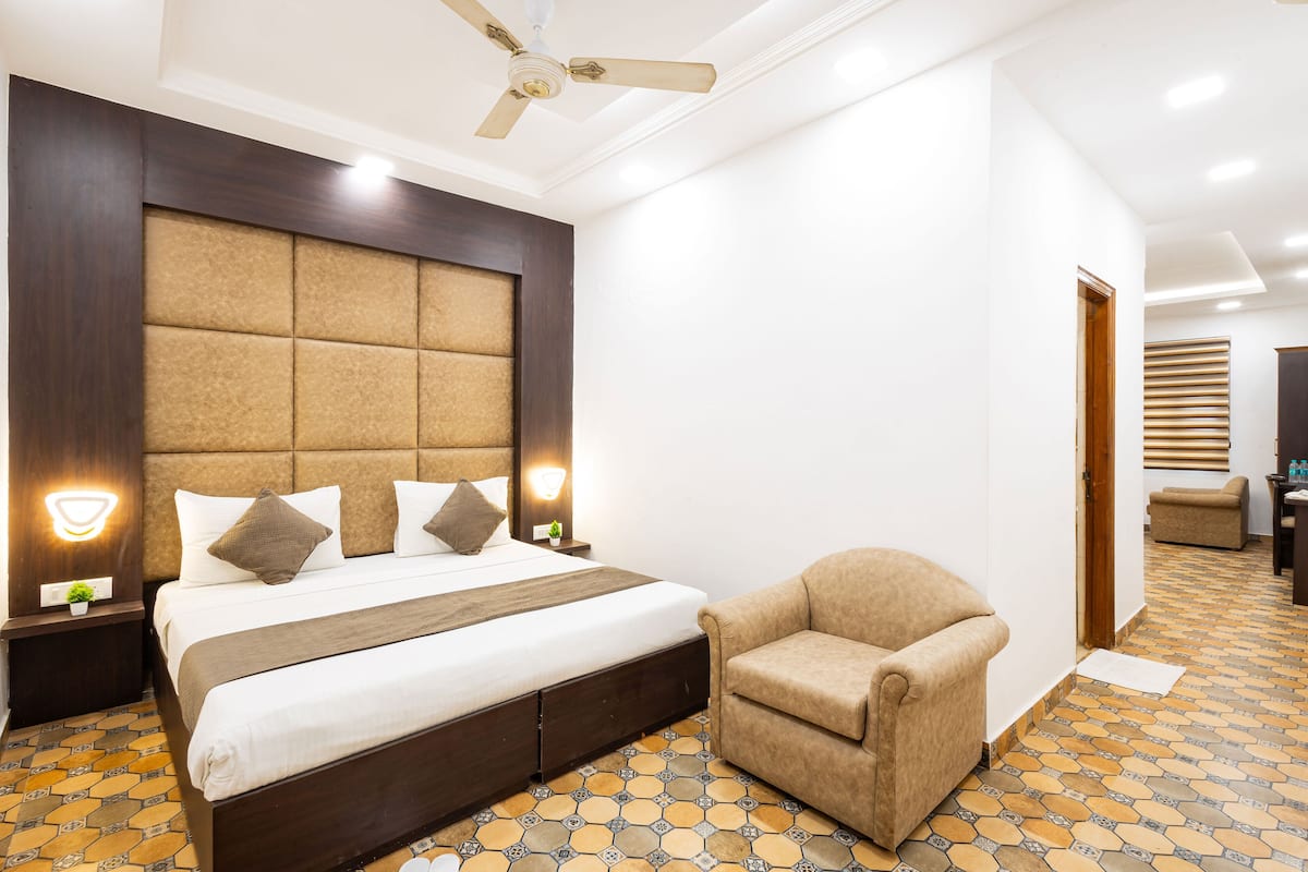 Quarto com cama grande, cabeceira, ventilador de teto, mesa de cabeceira, cadeira e piso estampado.