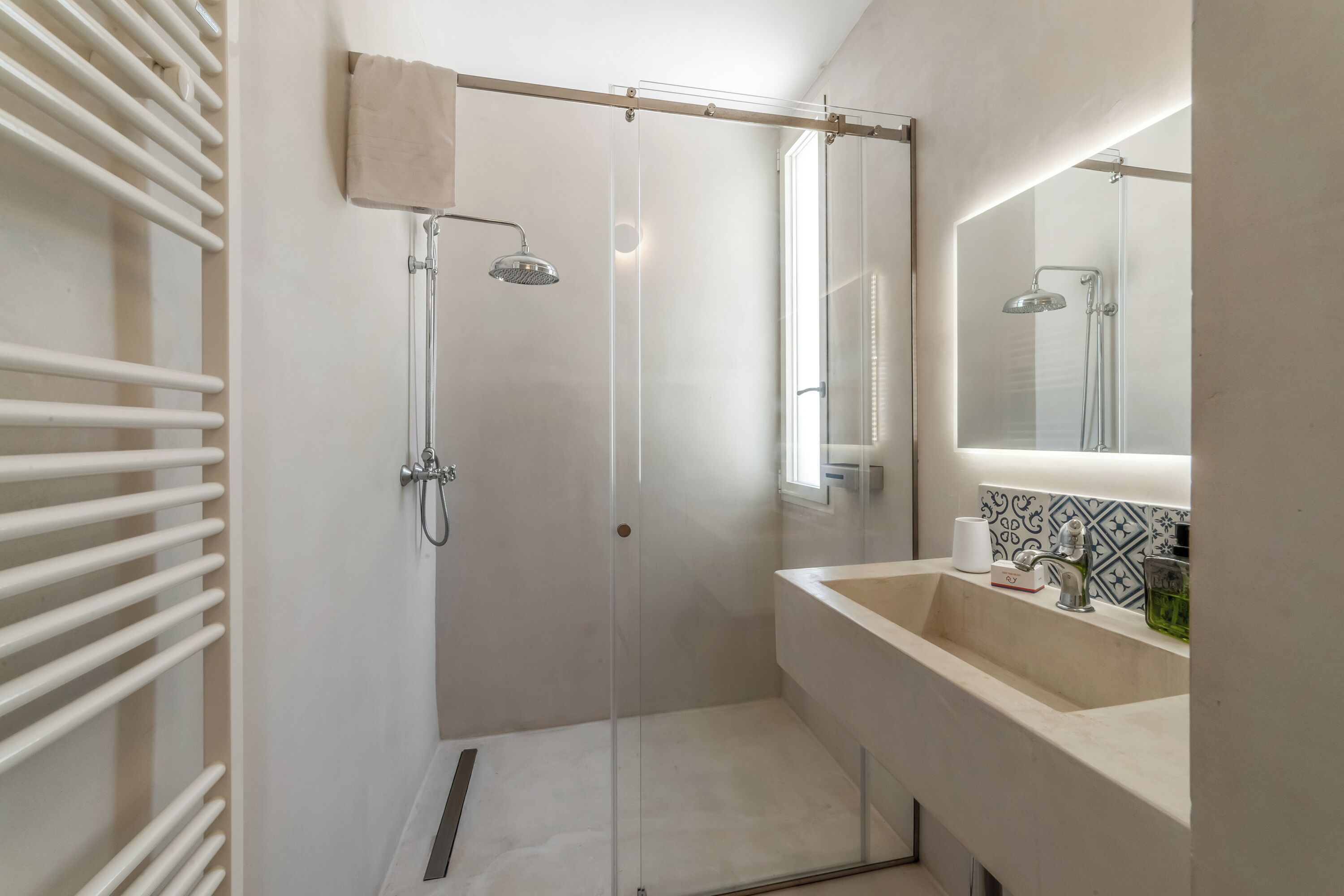 Uma casa de banho moderna com cabine de duche em vidro, uma sanita branca com espelho em cima e um porta-toalhas à esquerda.