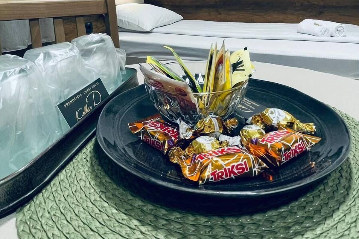 Quarto de hotel com uma cama, uma mesa de cabeceira com um recipiente de vidro cheio de chocolates e duas fotografias emolduradas na parede.