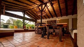 Um interior rústico com soalho de azulejos, mobiliário de madeira e um telhado de palha.