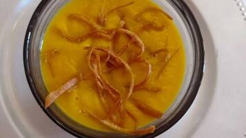 Uma tigela de sopa com caldo transparente e guarnecida com palha de batata crocante, servida em um prato branco com borda decorativa.