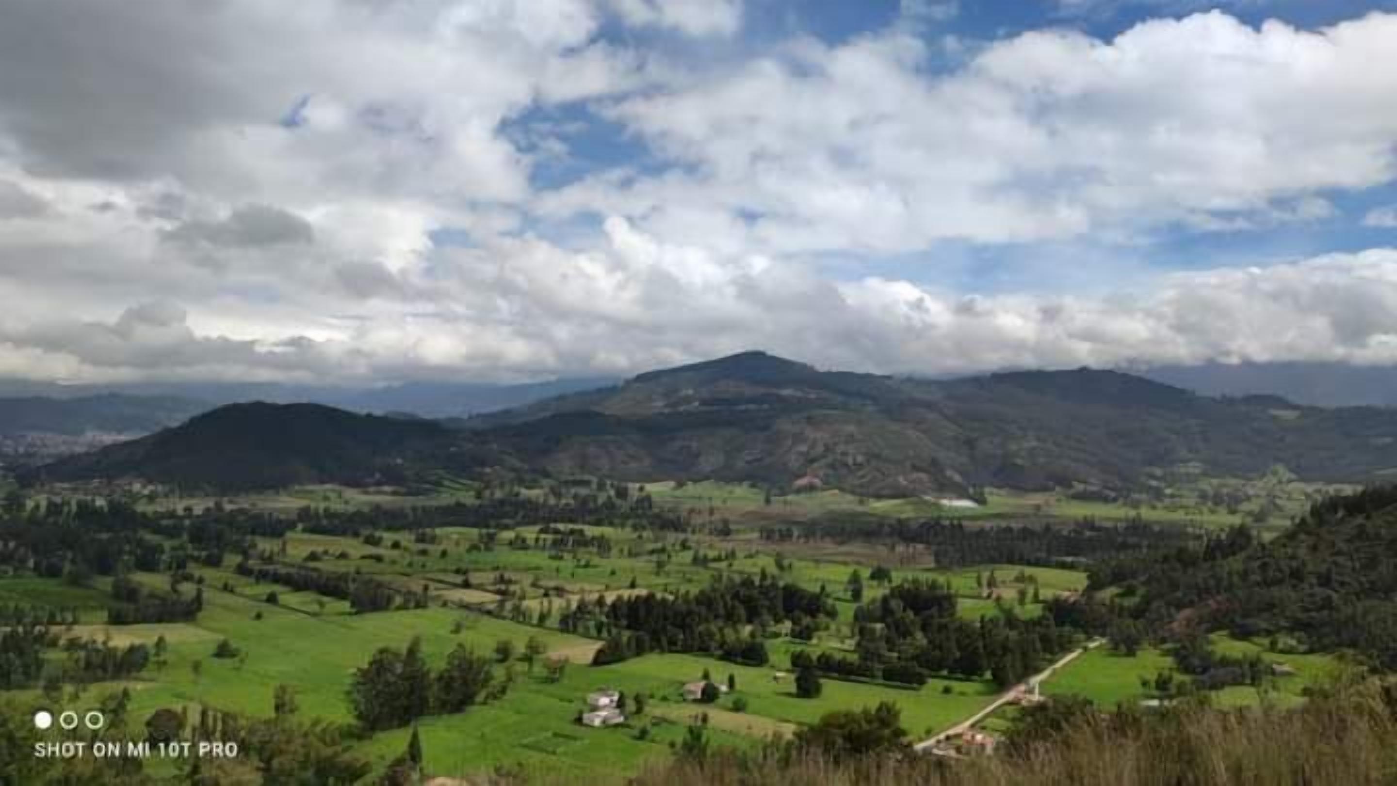 Uma vista panorâmica de uma paisagem montanhosa com campos verdes e edifícios dispersos.