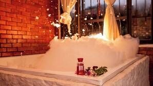 Uma banheira cheia de neve, uma garrafa de líquido vermelho e algumas flores num parapeito.