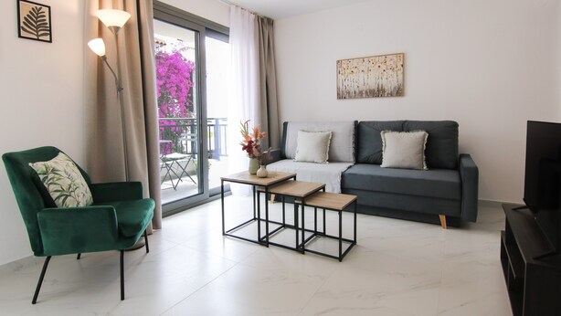 Uma sala de estar moderna com uma poltrona verde, um sofá cinzento, uma mesa de centro e uma televisão.