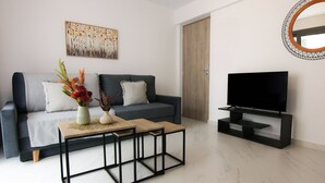 Uma sala de estar moderna com um sofá cinza, uma mesa de centro com vasos, uma televisão de tela plana em um suporte preto e uma porta de madeira.
