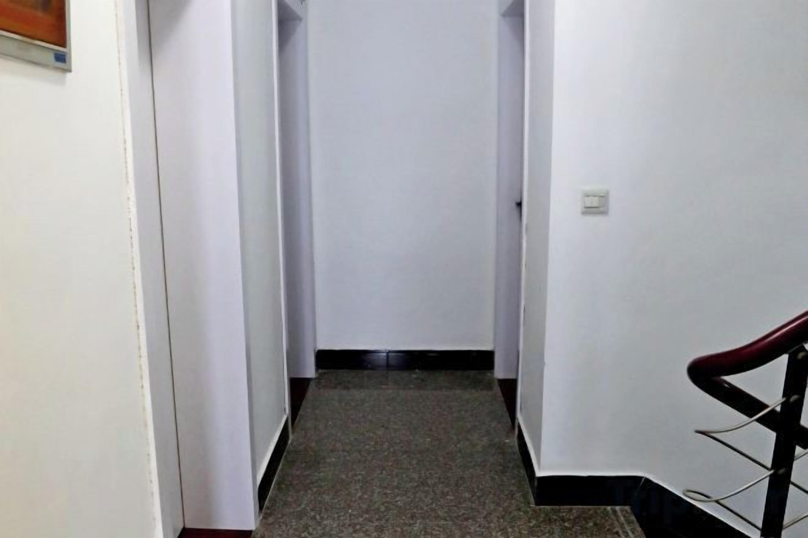 Um corredor estreito com carpete e corrimão à direita.
